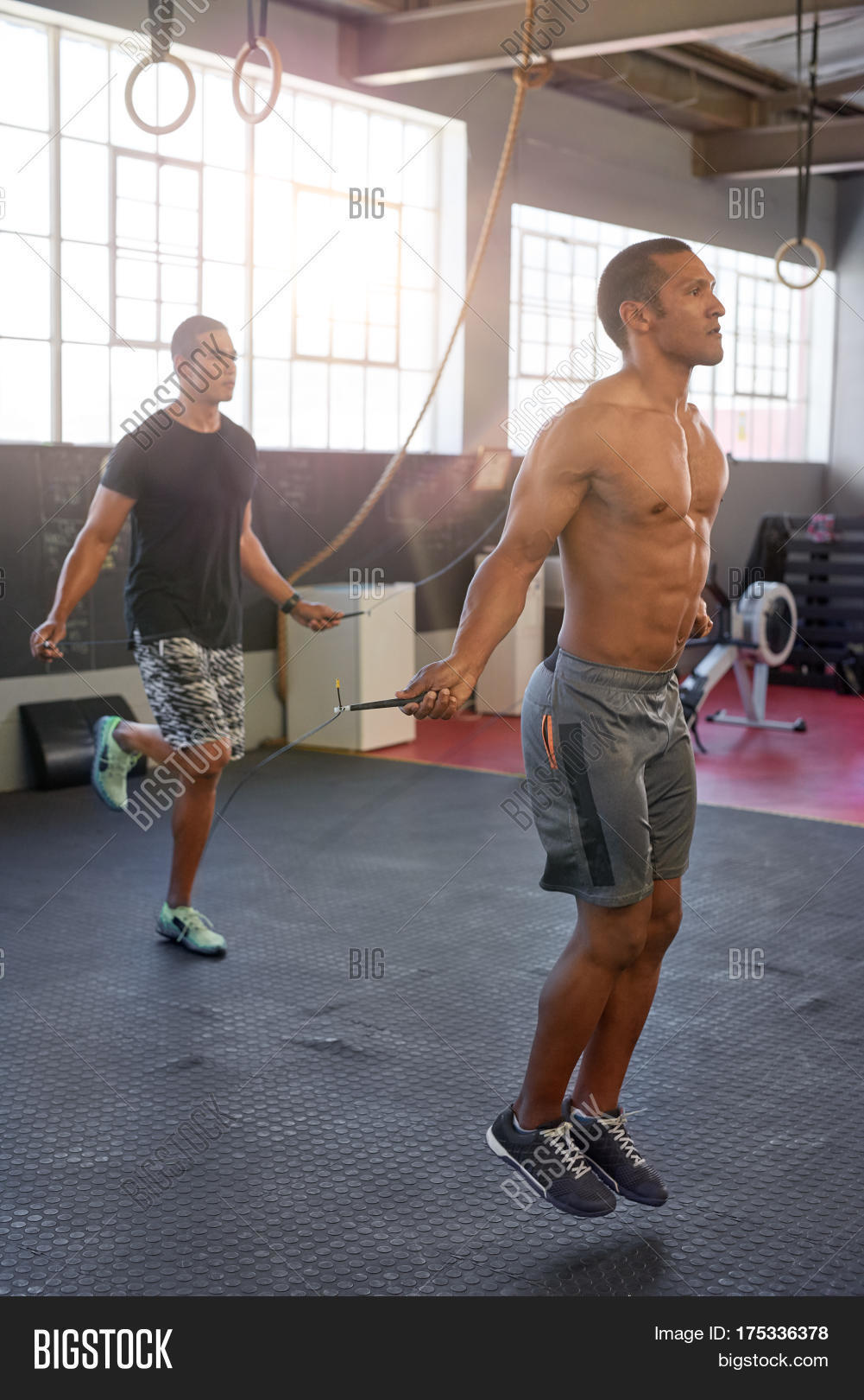 Strong muscular mixed race man jumping with skipping rope in gym warm ...
